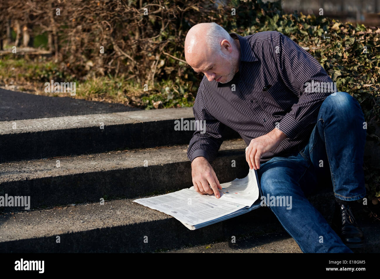 Man sitting on steps reading a newspaper Stock Photo - Alamy