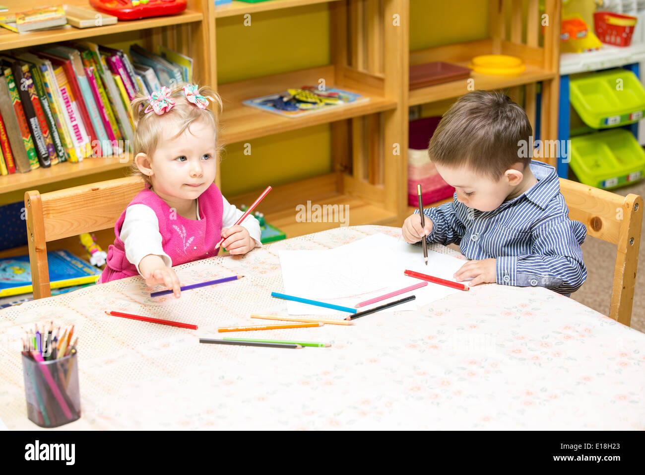 Two little kids drawing with colorful pencils in preschool at the table ...