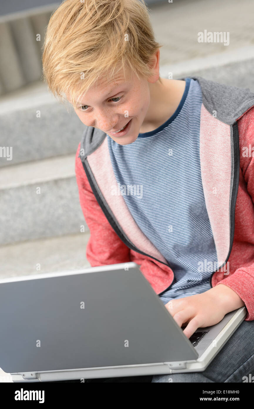 Surprised teenage student boy using laptop sitting outside on steps ...