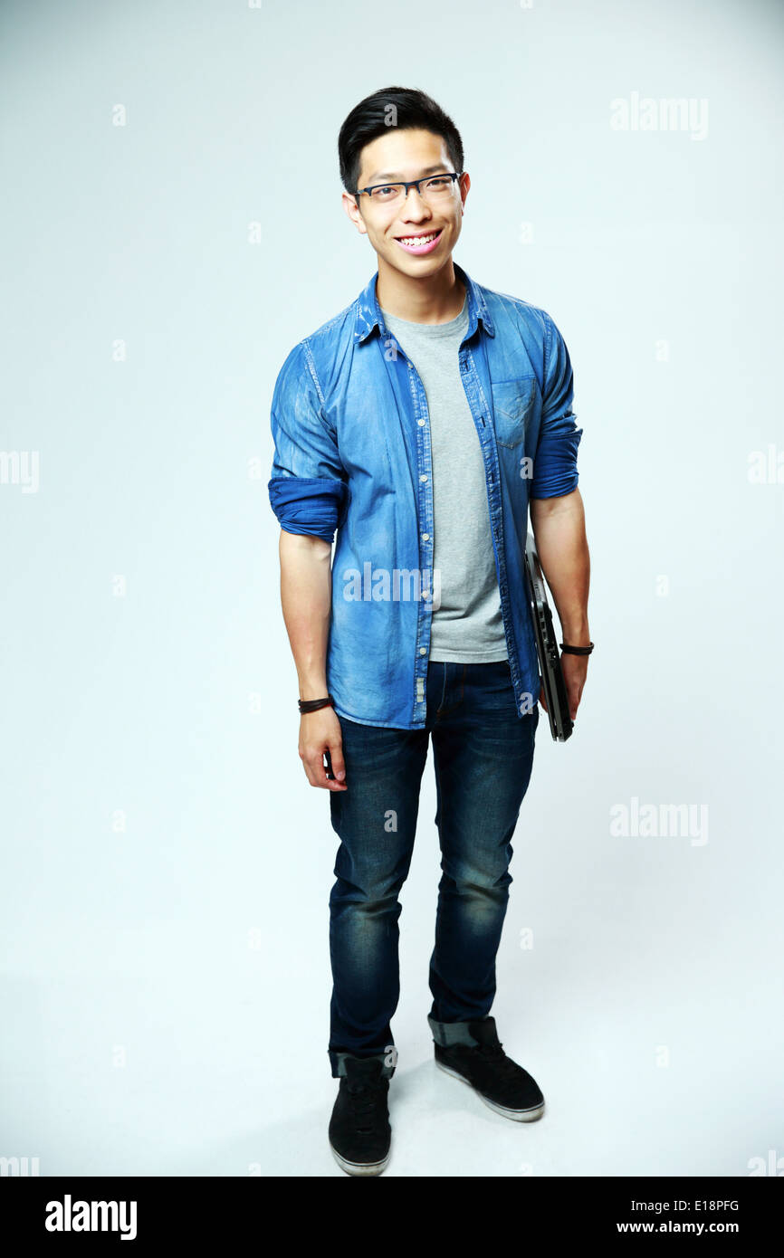 Full length portrait of a happy asian man standing with laptop on gray ...