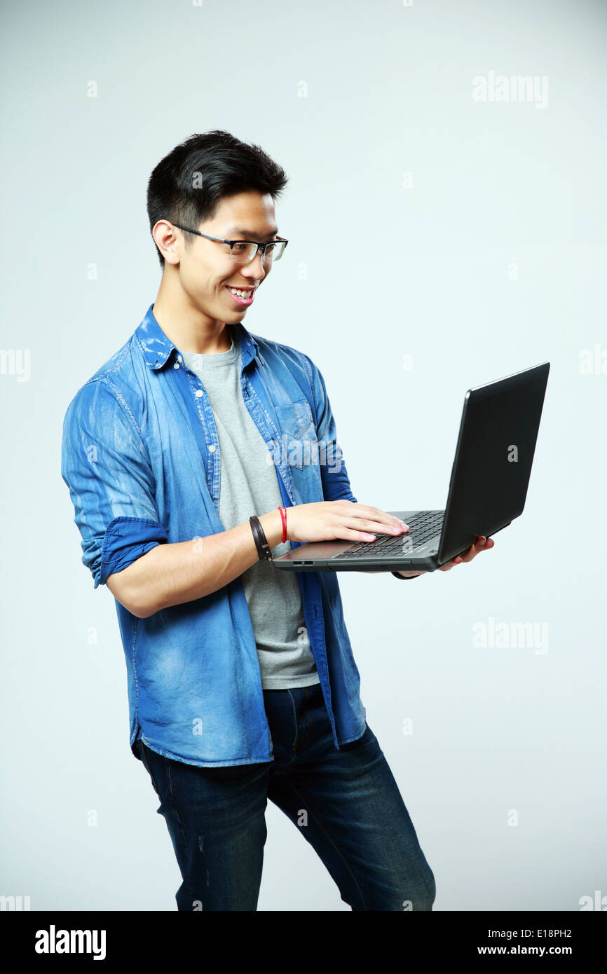 Happy asian man using laptop on gray background Stock Photo - Alamy