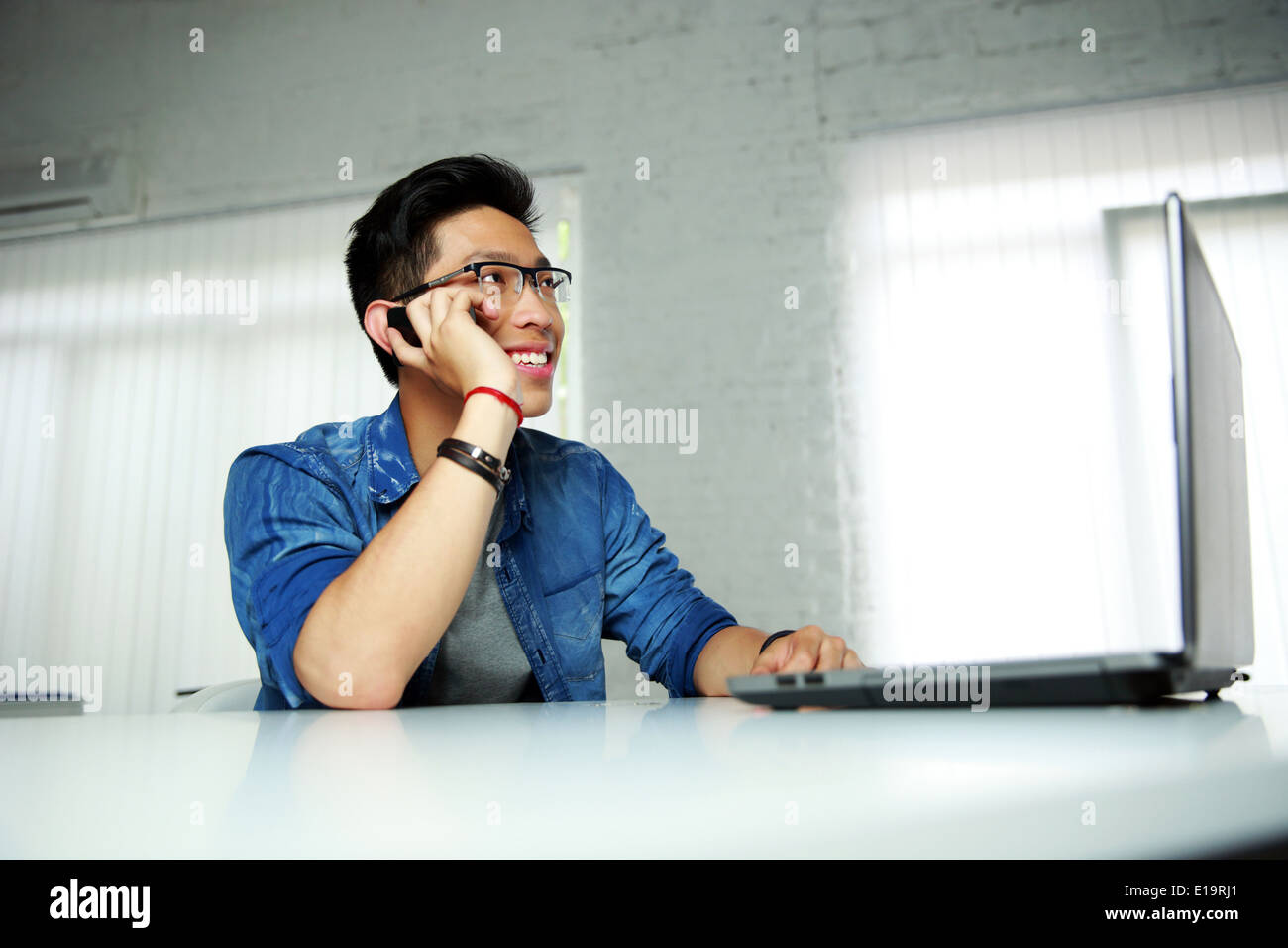 Happy asian man sitting at his workplace in office and talking on the phone Stock Photo - Alamy