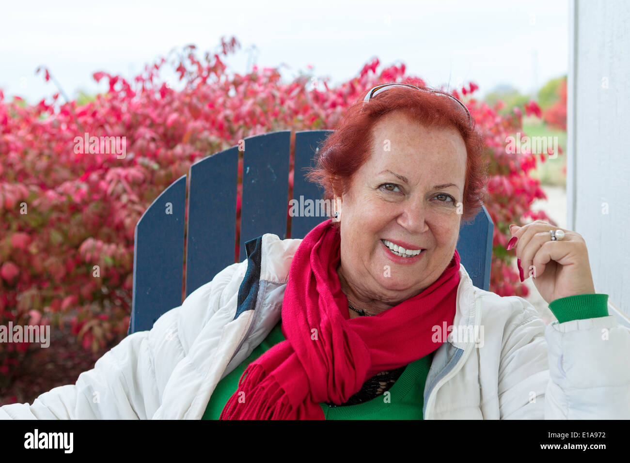 Red hair senior woman outside on a blue chair smiling large with her ...