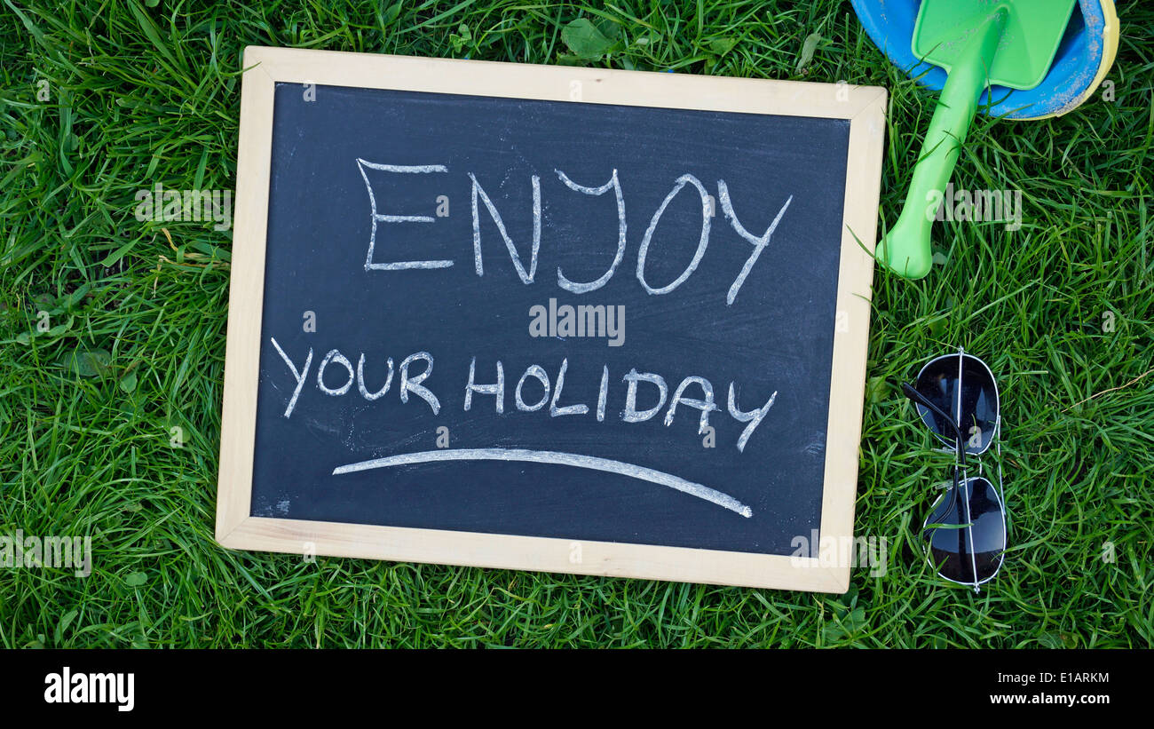 Enjoy your holiday written on a chalckboard with sunglasses and child ...