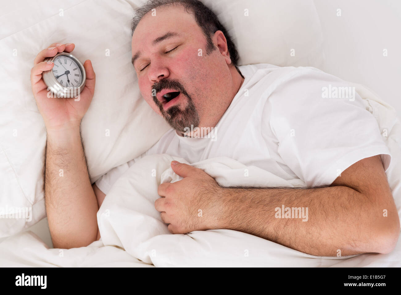 Lethargic tired man lying in bed yawning as he struggles to wake up ...