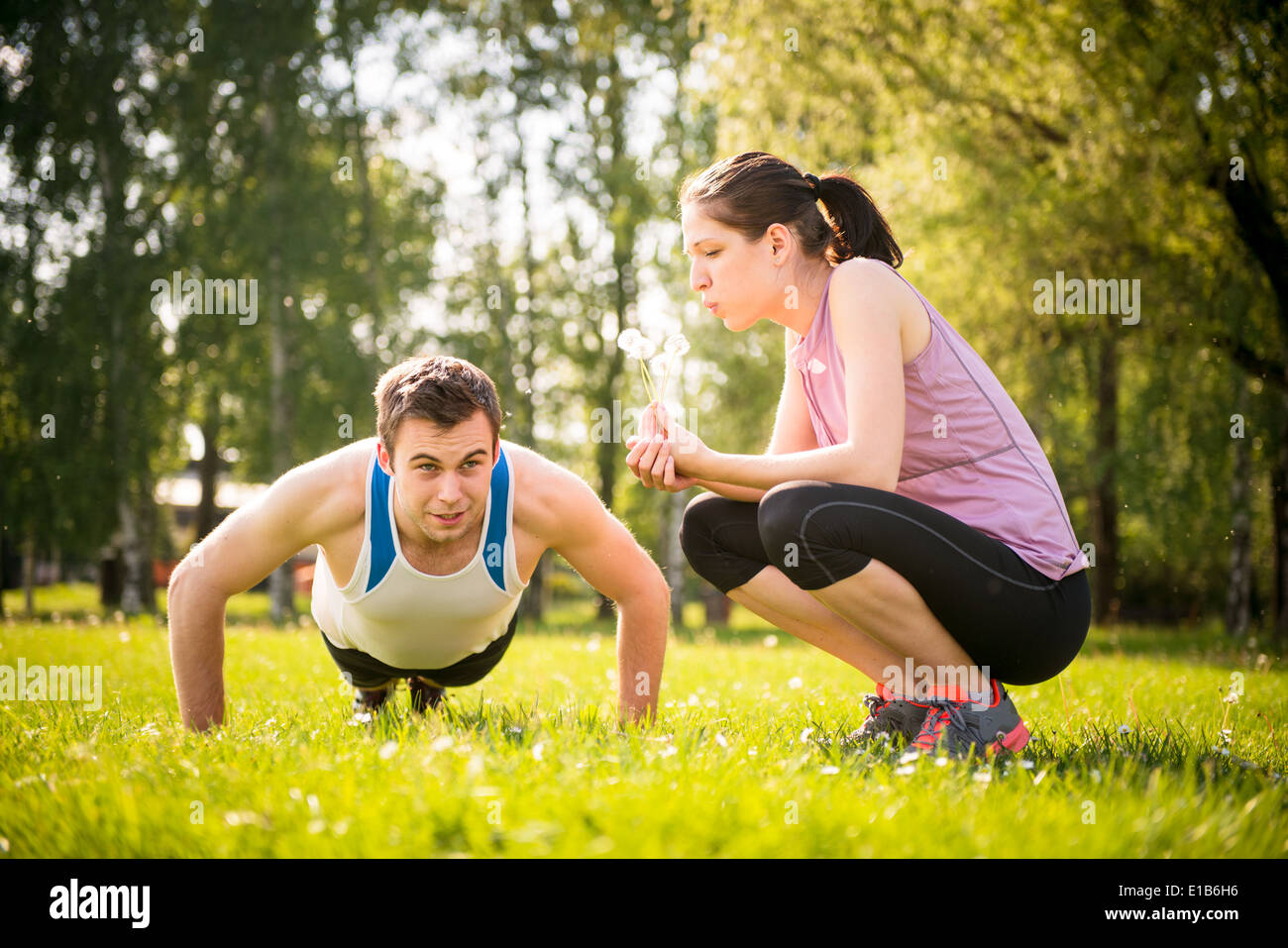 Man making push-ups while woman is blowing dandelion seeds on him ...