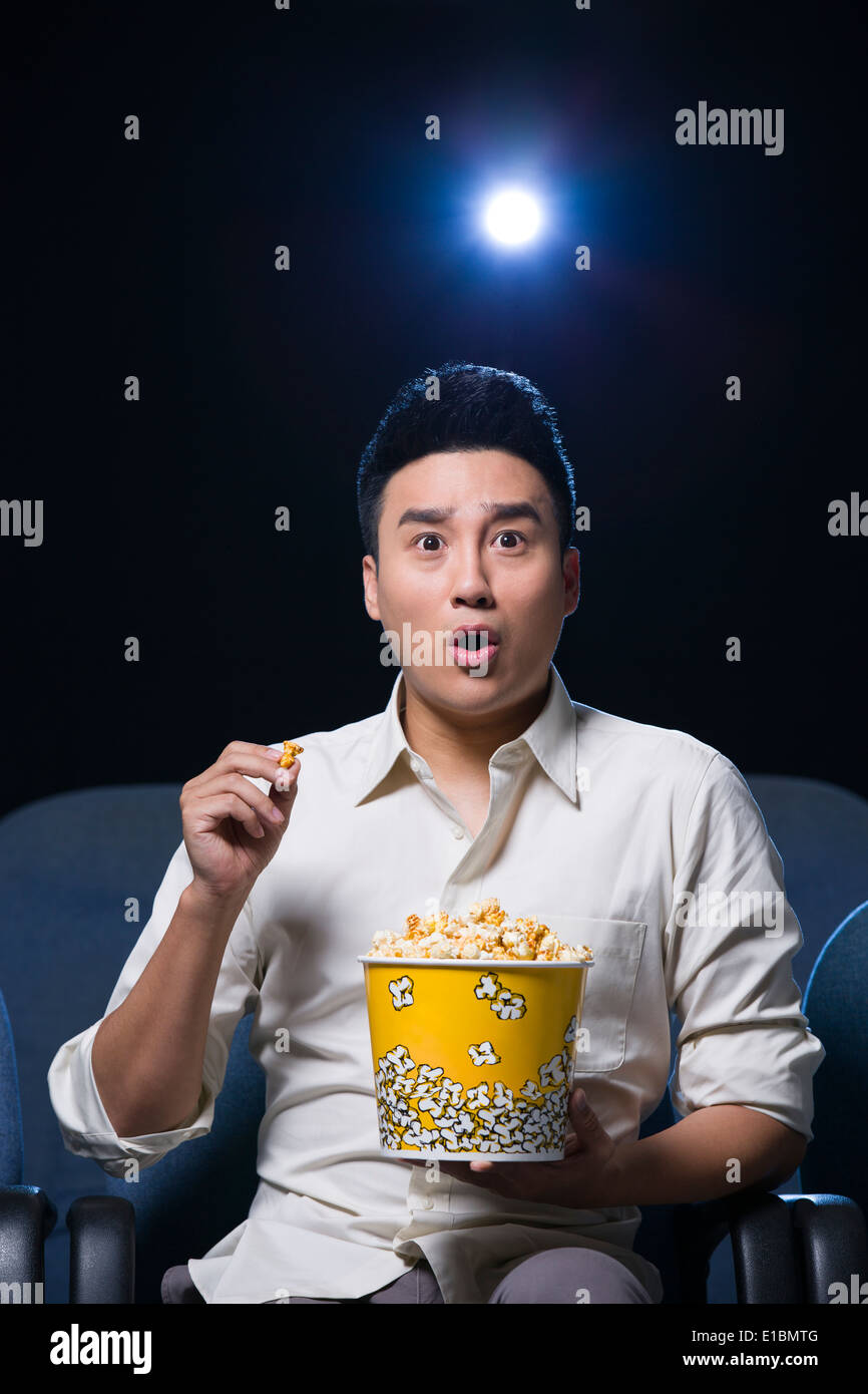 Young man watching horrible movie in cinema Stock Photo - Alamy