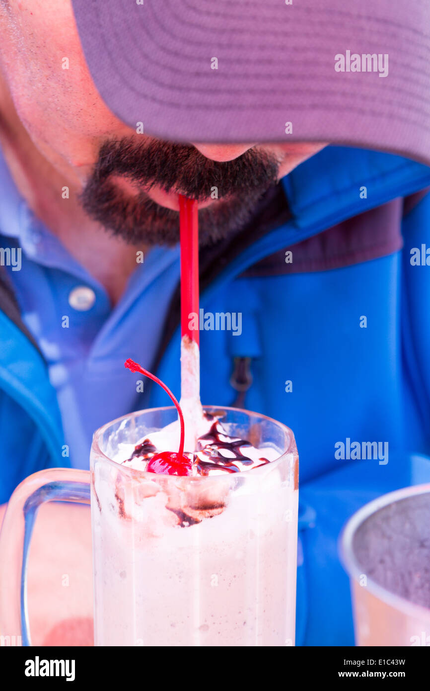 Man with a goatee beard bending forwards in a peak cap drinking a ...
