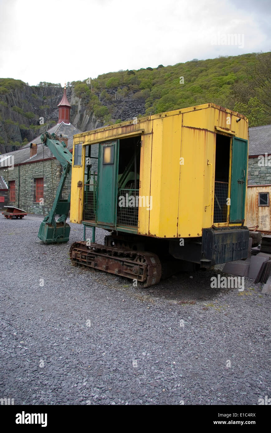Yellow steam shovel with green bucket on rusty tracks with buildings ...