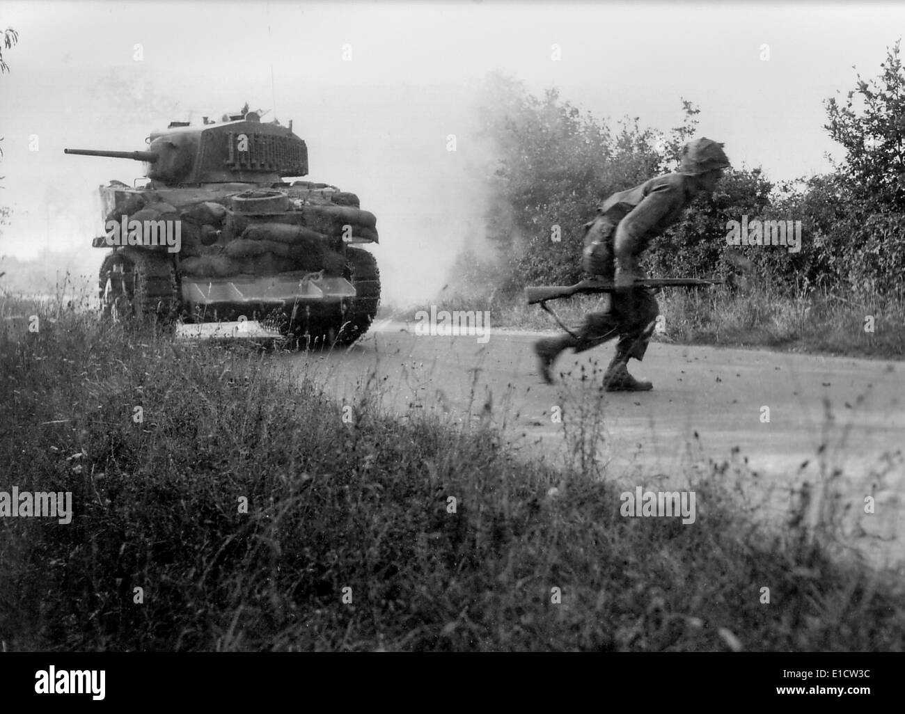 U.S. soldier crosses a road cautiously under the cover of a light tank ...