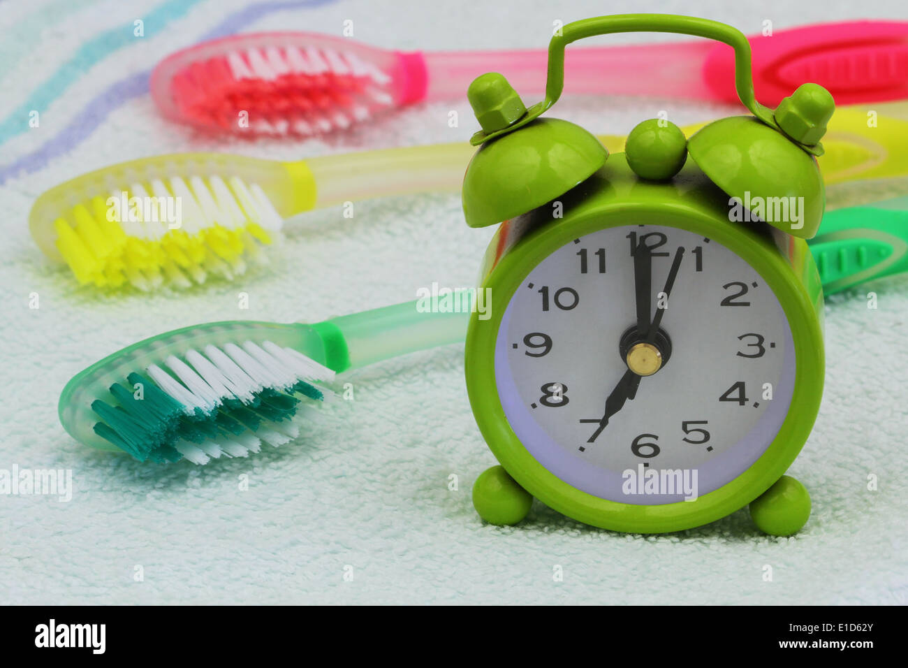 Miniature clock showing 7 am with colorful toothbrushes Stock Photo - Alamy