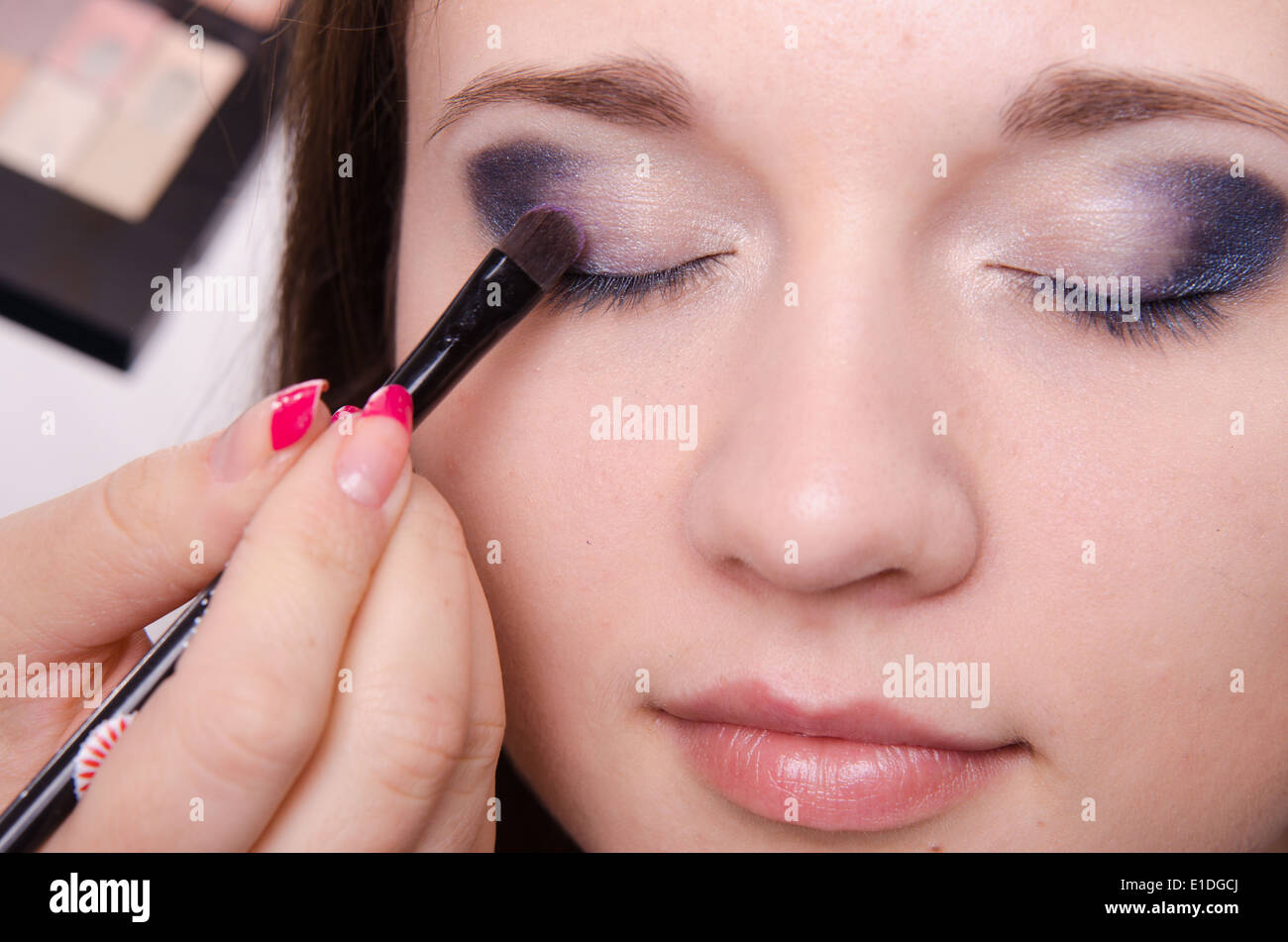Makeup artist paints the eyelids of a beautiful young girl in the ...