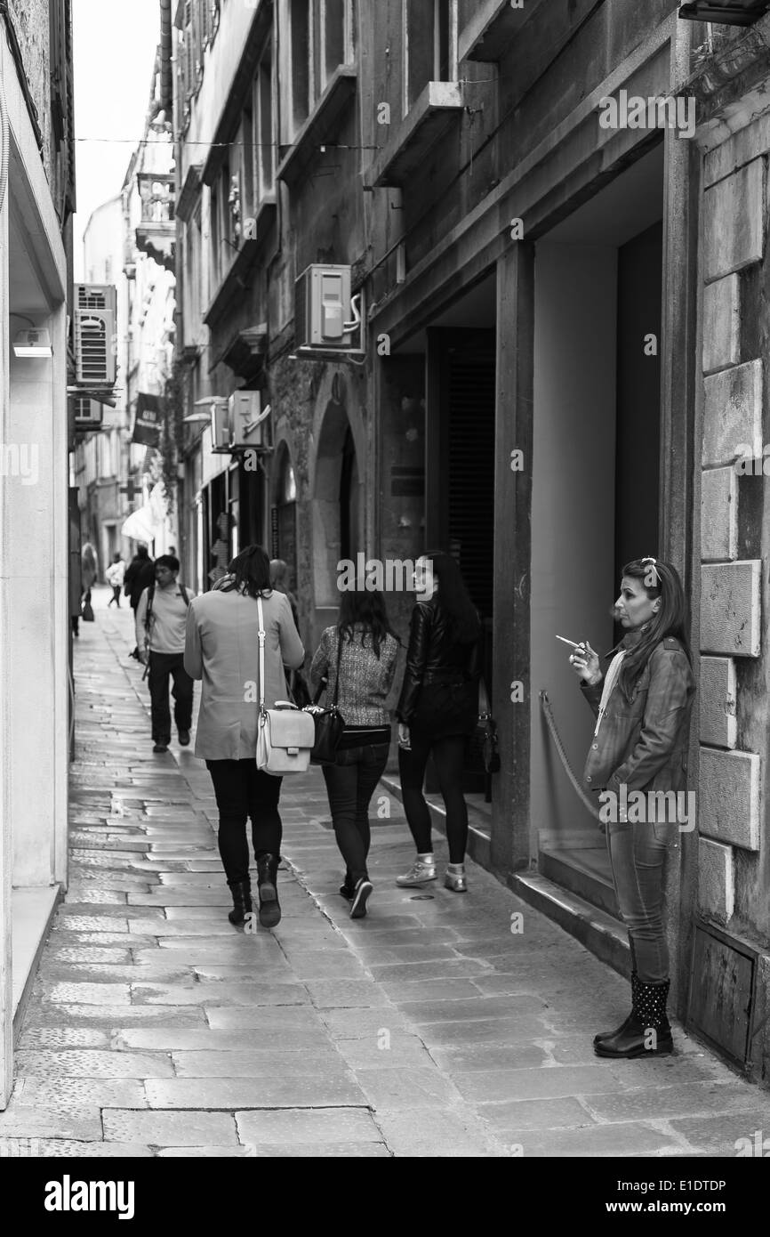 A woman is stood smoking a cigarette outside a store in a street in the ...