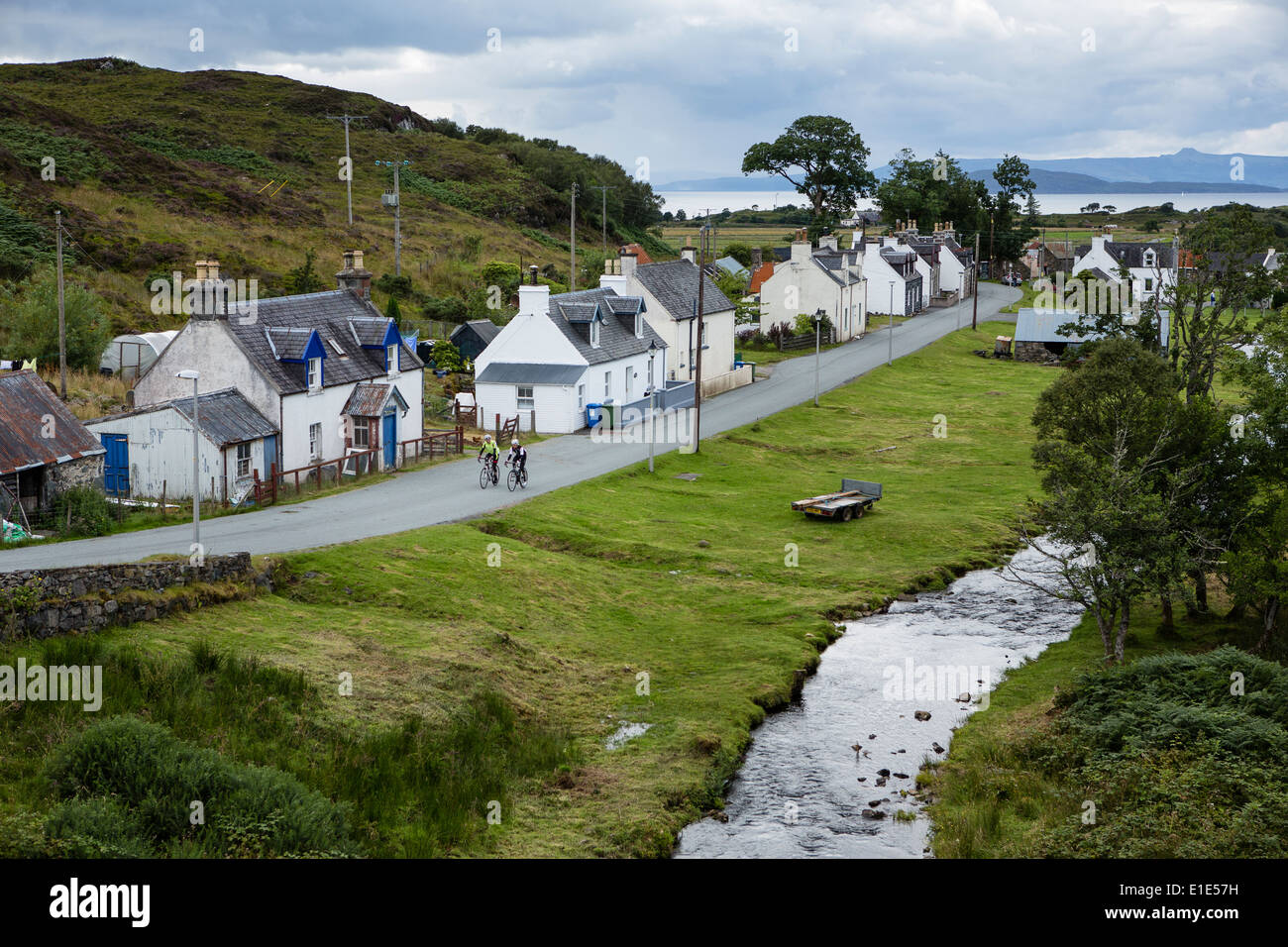 Pair of cyclists ride a path through a village on the Isle of Skye ...