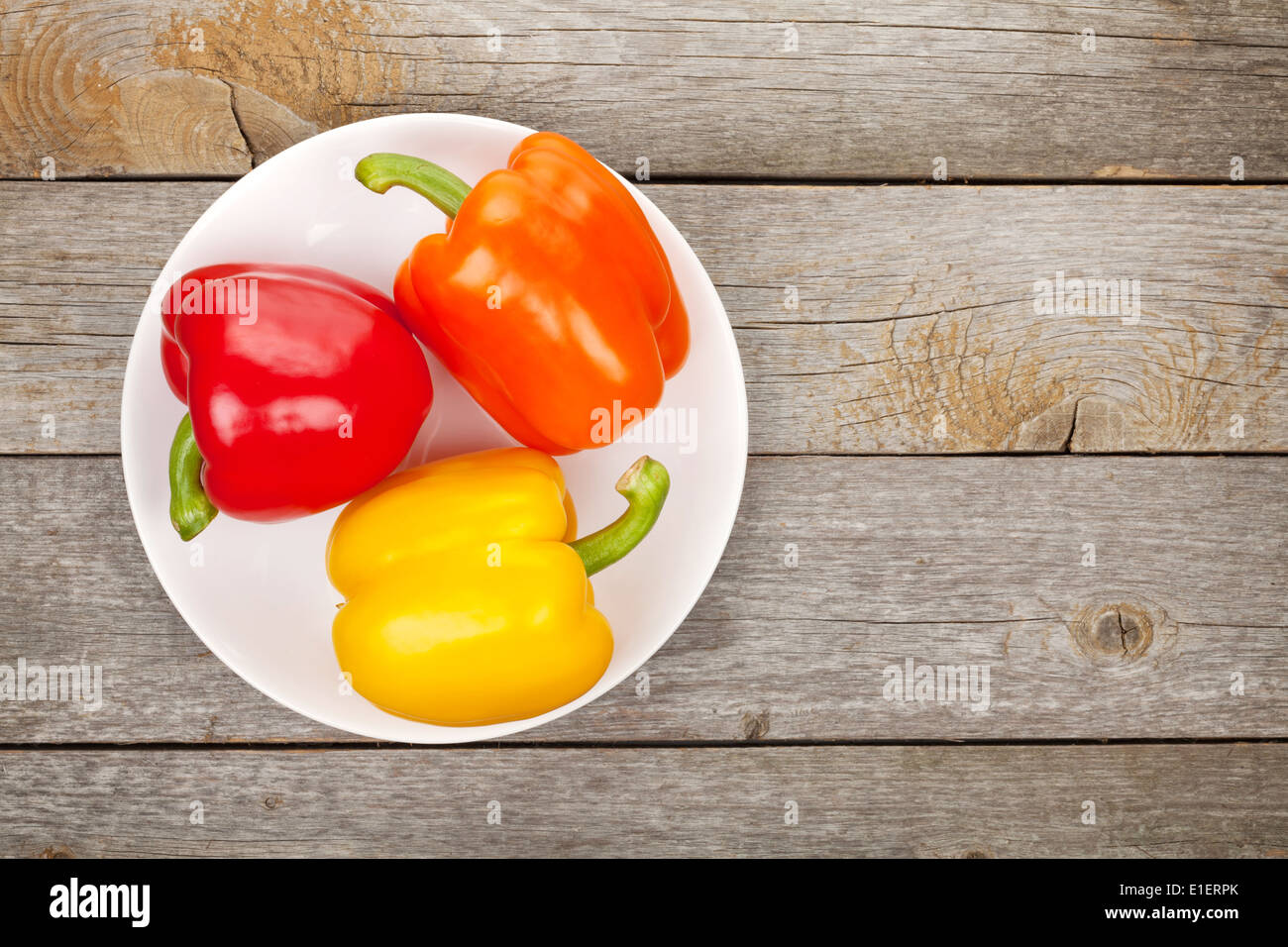 Colorful bell peppers on plate over wooden table background with copy ...