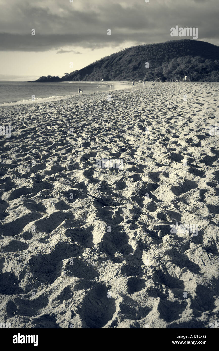 A wide expansive sand beach with dark clouds and a mountain in the ...