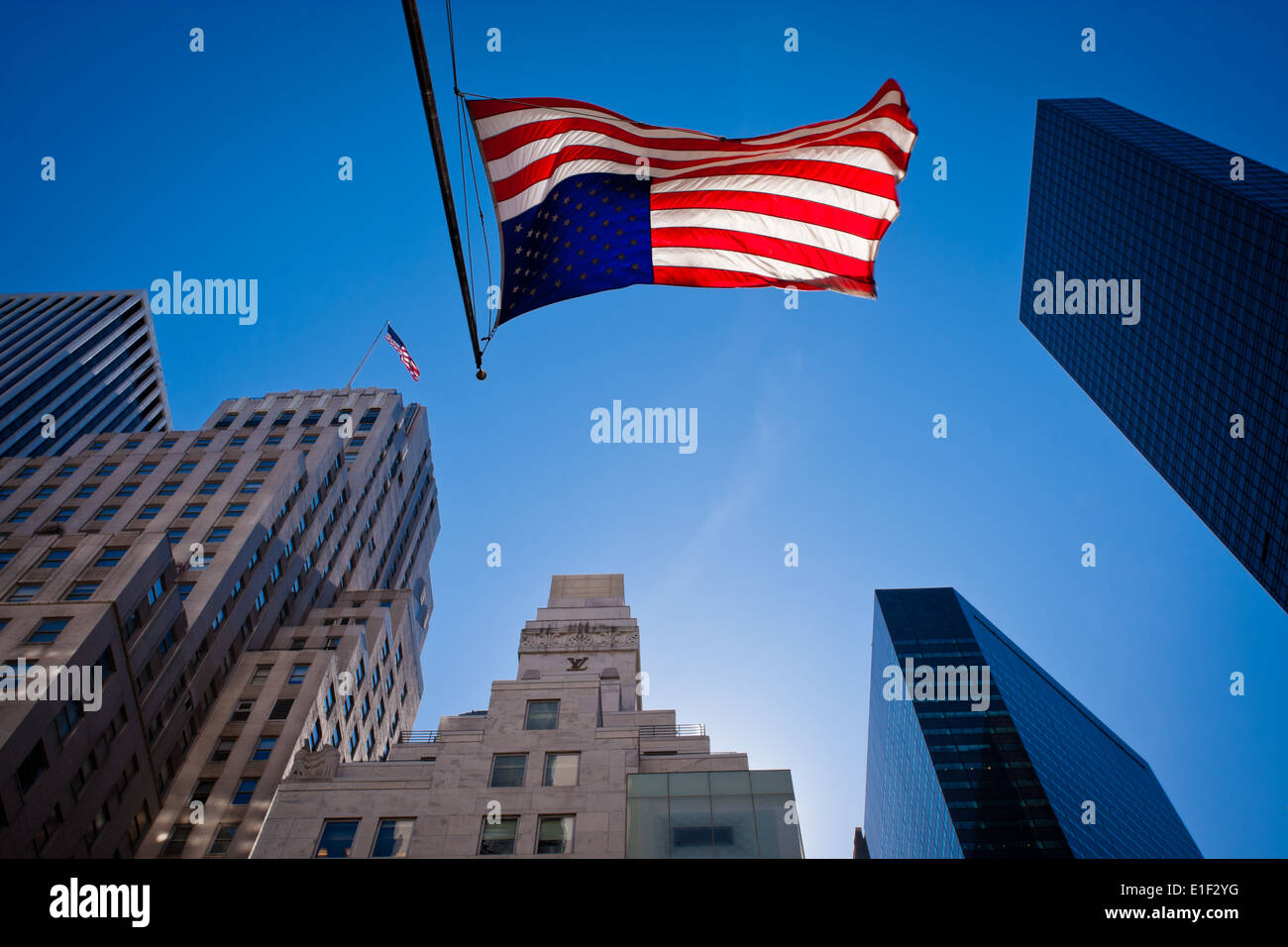 US flag flying against a bright blue sky and tall skyscrapers around it ...