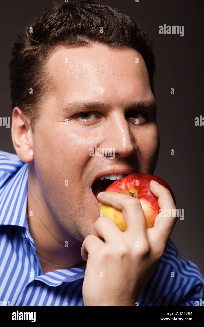 Diet and nutrition. Happy young man eating apple seasonal fruit on dark ...