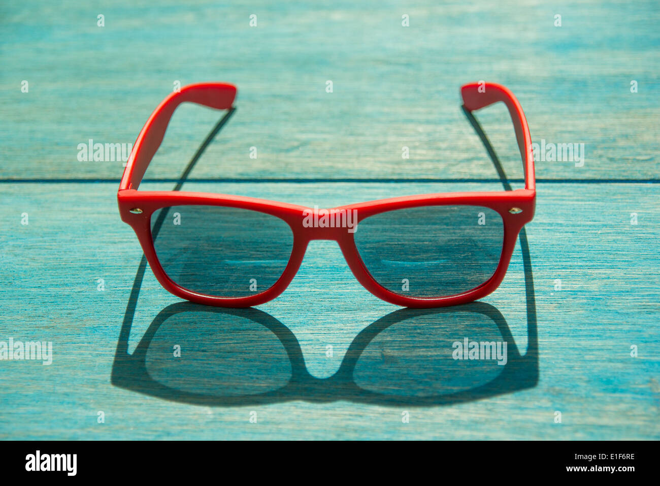 Red sunglasses over a blue wood background with a shadow caused by the ...