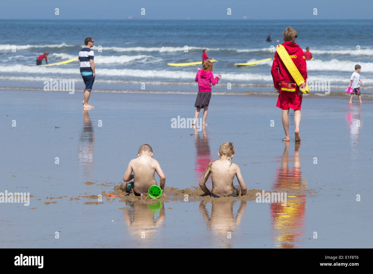 Two young boys playing on beach as lifeguard patrols beach as surfers ...