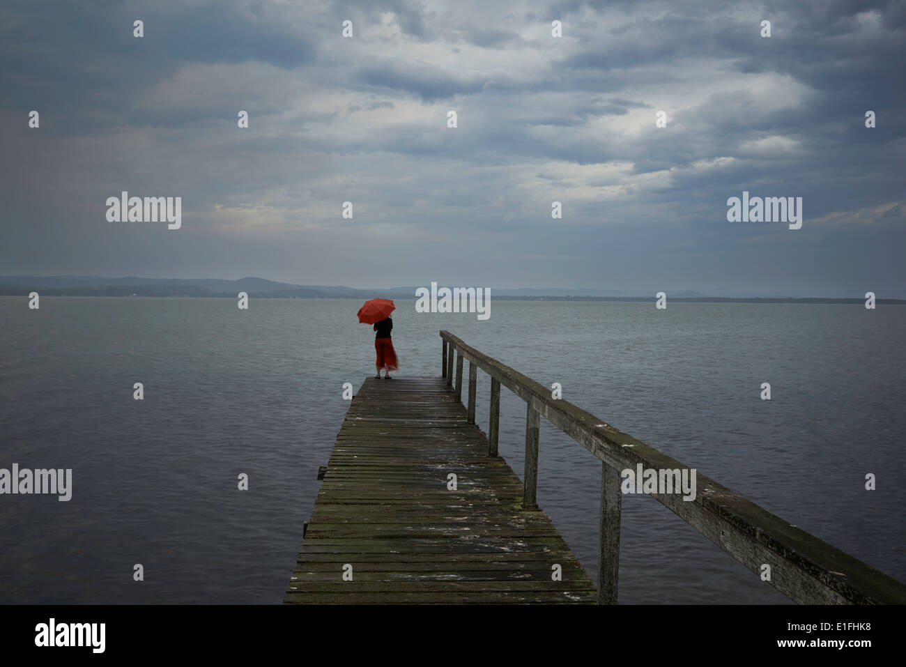 Lady with red umbrella at end of jetty with impending thunderstorm ...