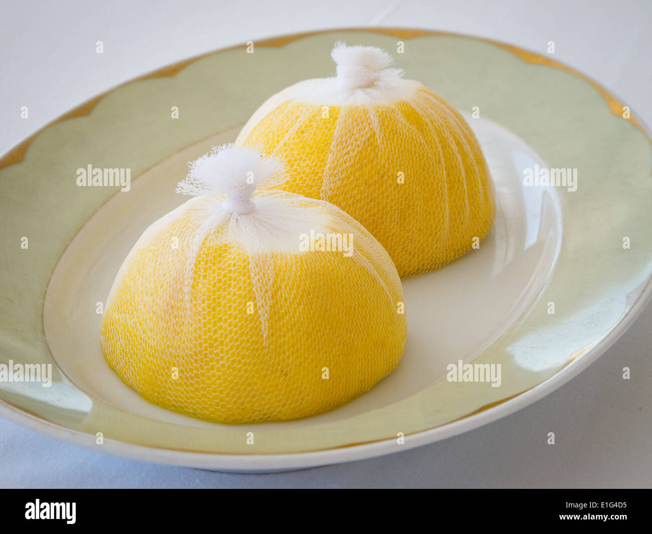 Lemons served in netting to catch the pips, on a china plate on a white ...