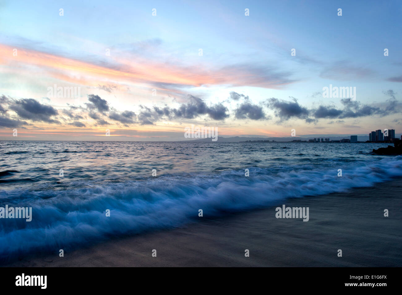 A city ocean sunset with a rolling wave and buildings on the skyline ...