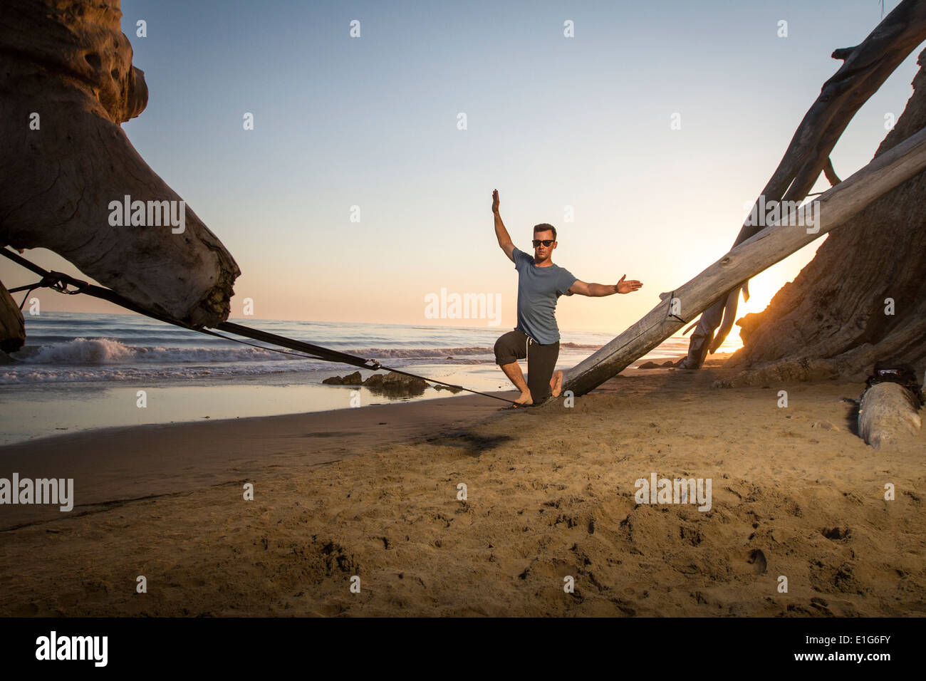 Athletic man in his twenties walking a slackline on the beach during ...