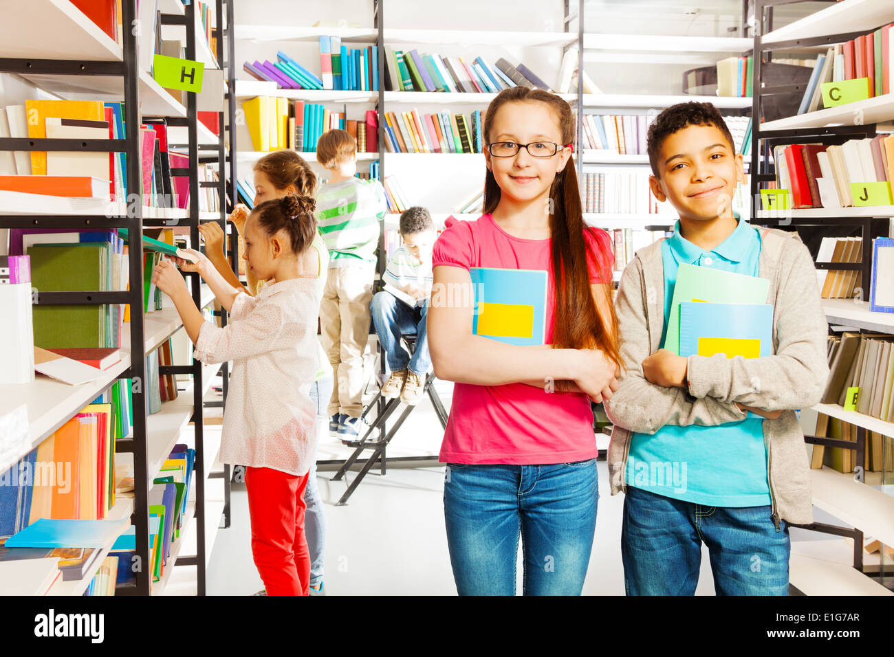 Happy kids in library stand together with books Stock Photo - Alamy