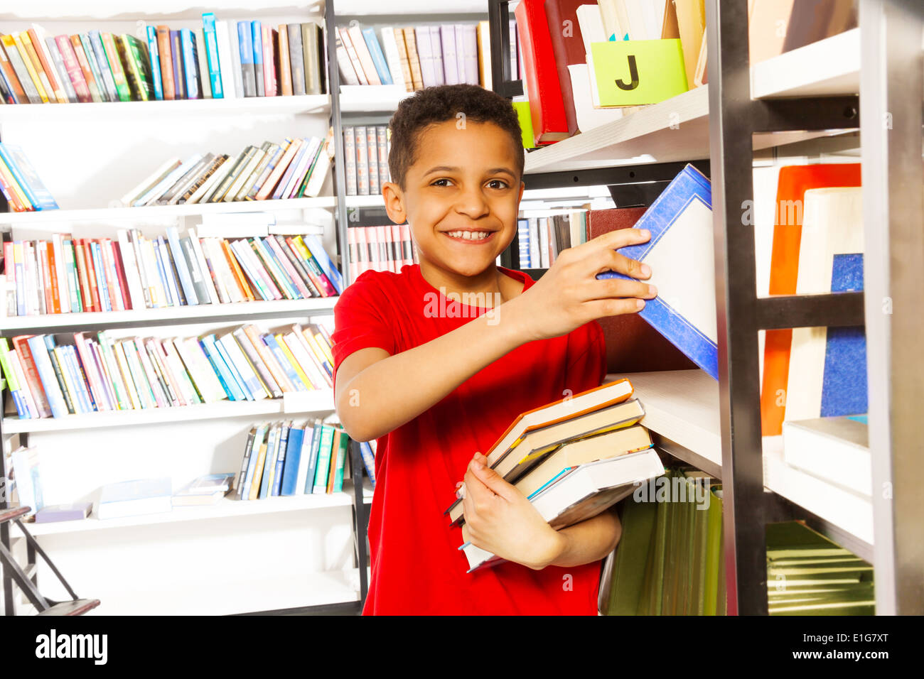 Happy boy with hand on bookshelf holds many books Stock Photo - Alamy