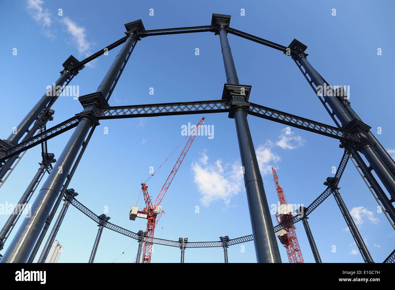 Skeletal gasometer frame and red cranes against blue sky with small ...