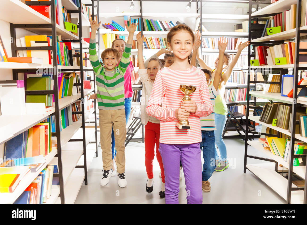 Happy girl holds golden cup, kids jumping behind Stock Photo - Alamy