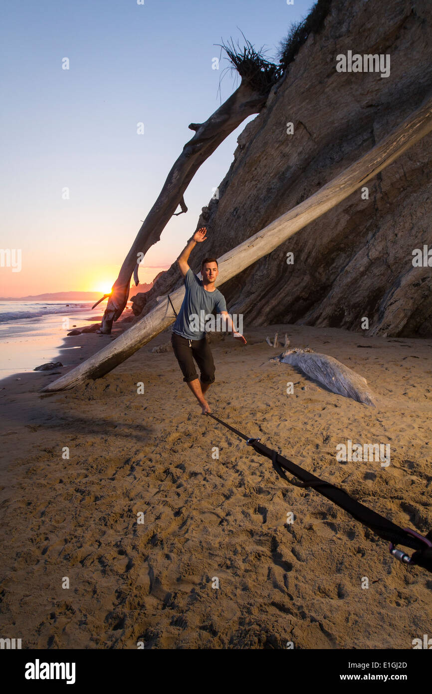 Athletic man in his twenties walking a slackline on the beach during ...