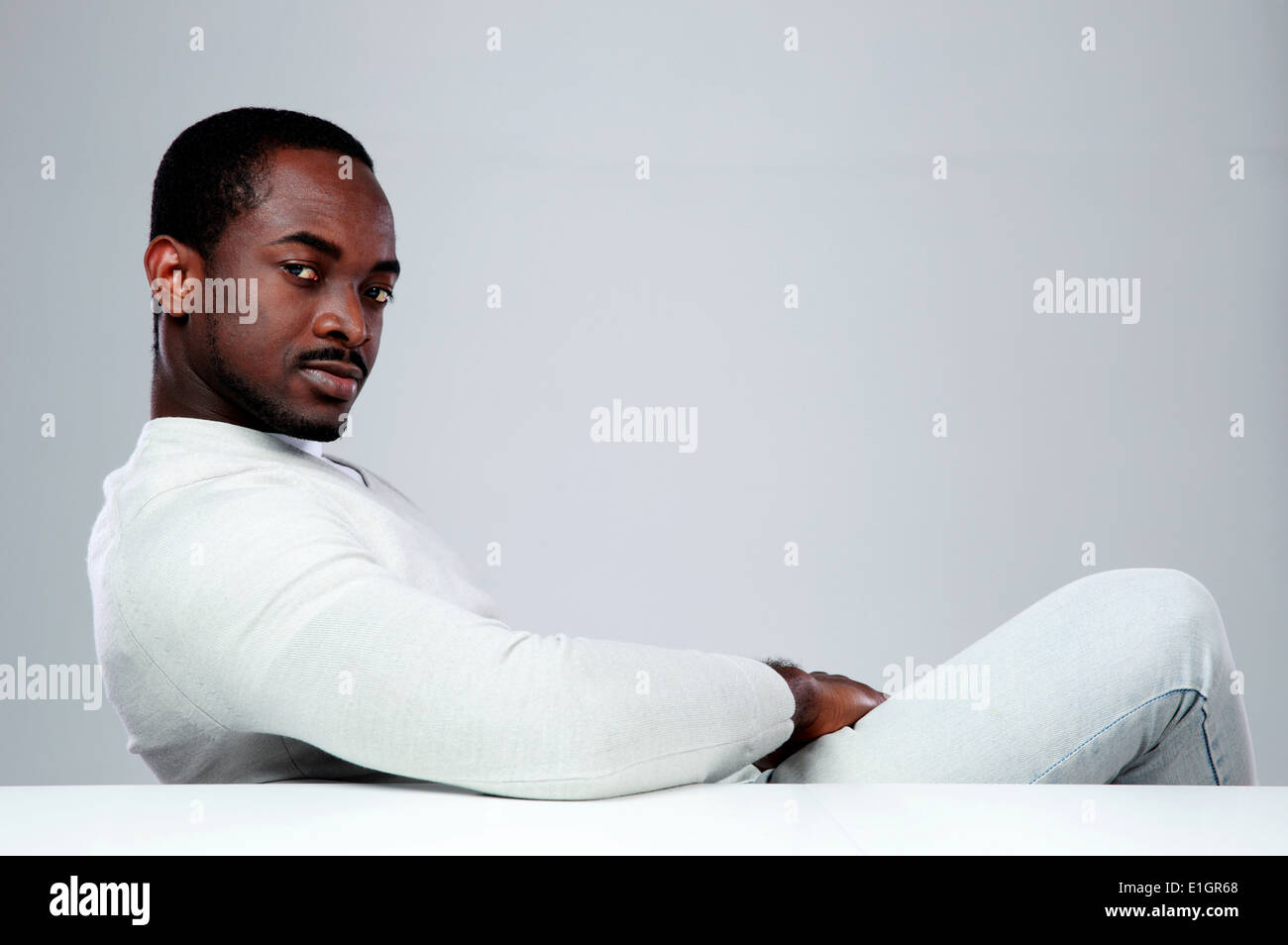Serious african man sitting at the table on gray background Stock Photo ...