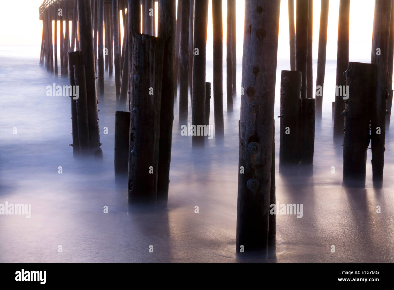 Waves breaking at sunrise under a pier at the beach Stock Photo - Alamy