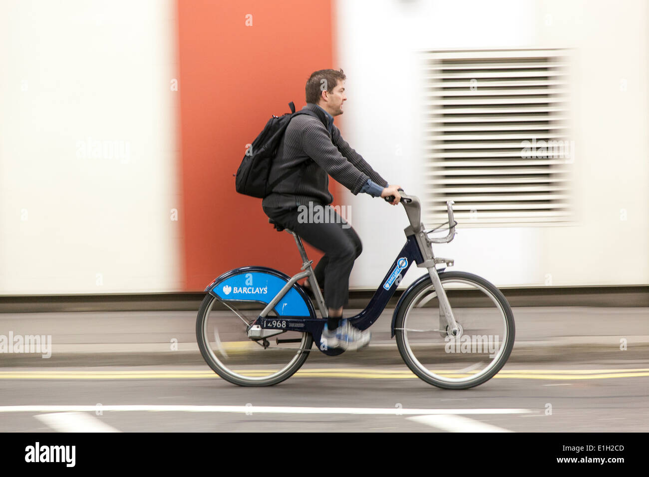 Man with a backpack rides a 'Boris bike' at speed Stock Photo - Alamy
