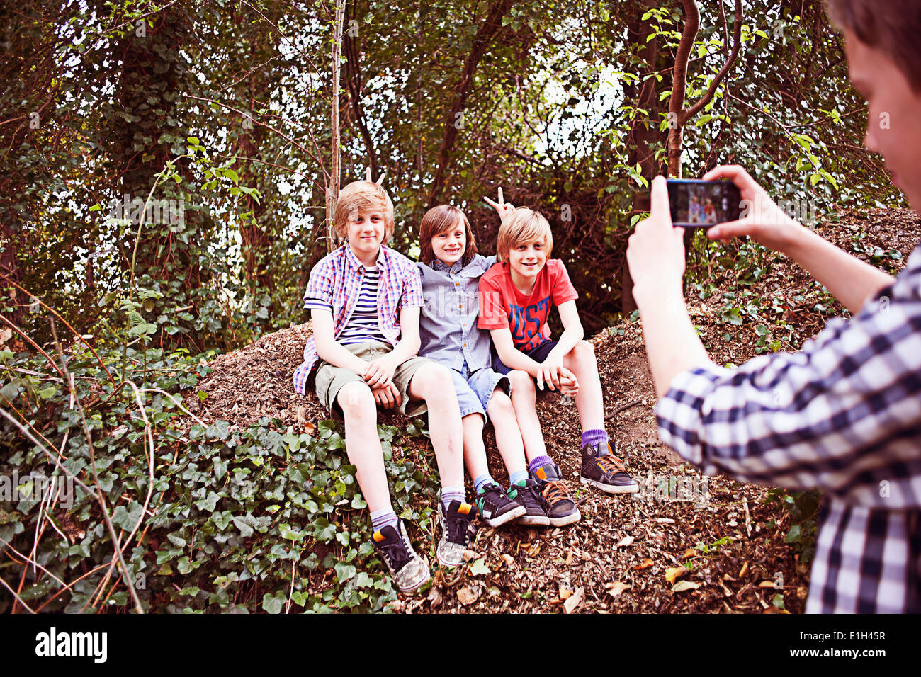 Boy photographing friends with phone in forest Stock Photo - Alamy