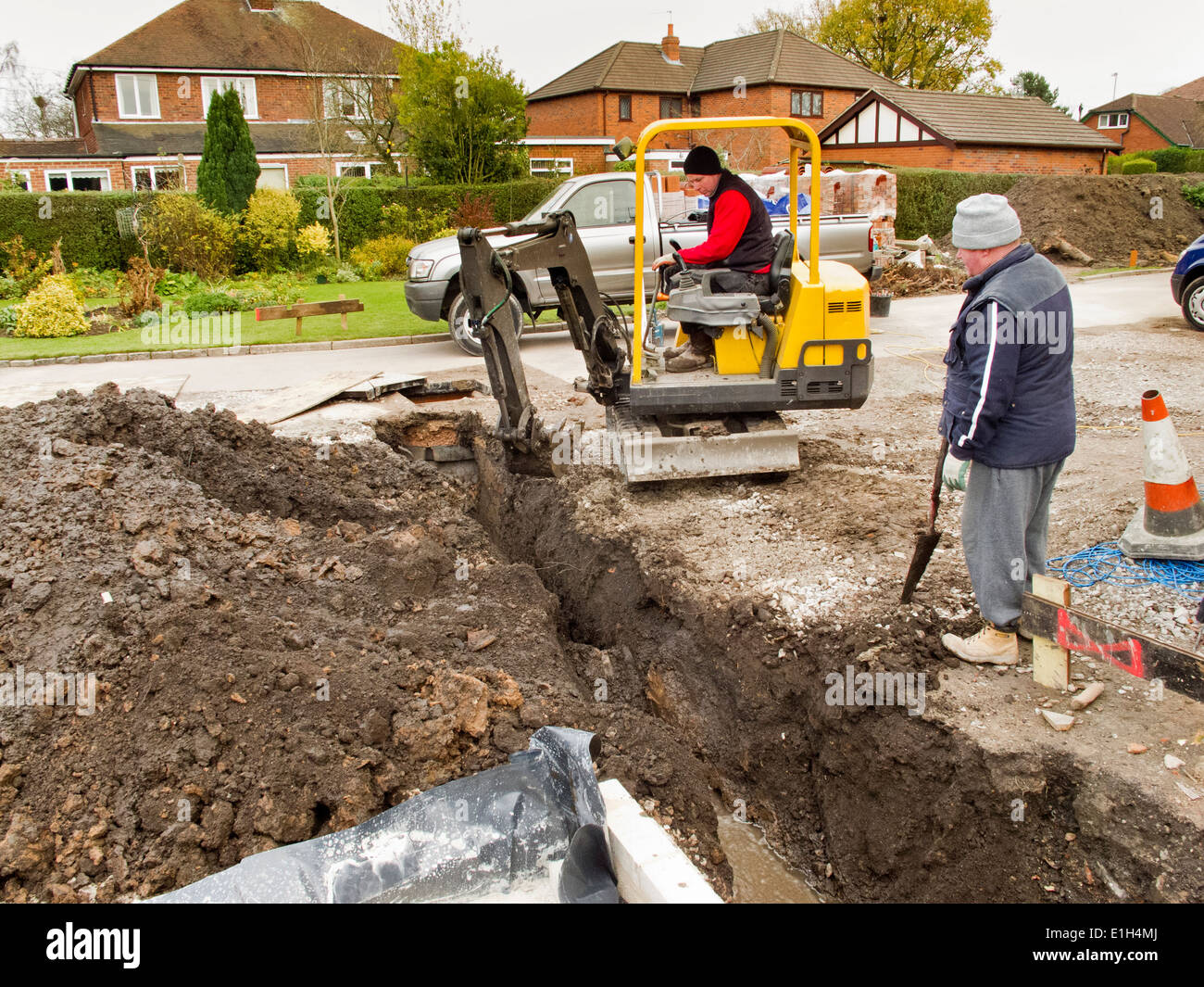 self building house, men excavating ditches for drains with mini digger ...