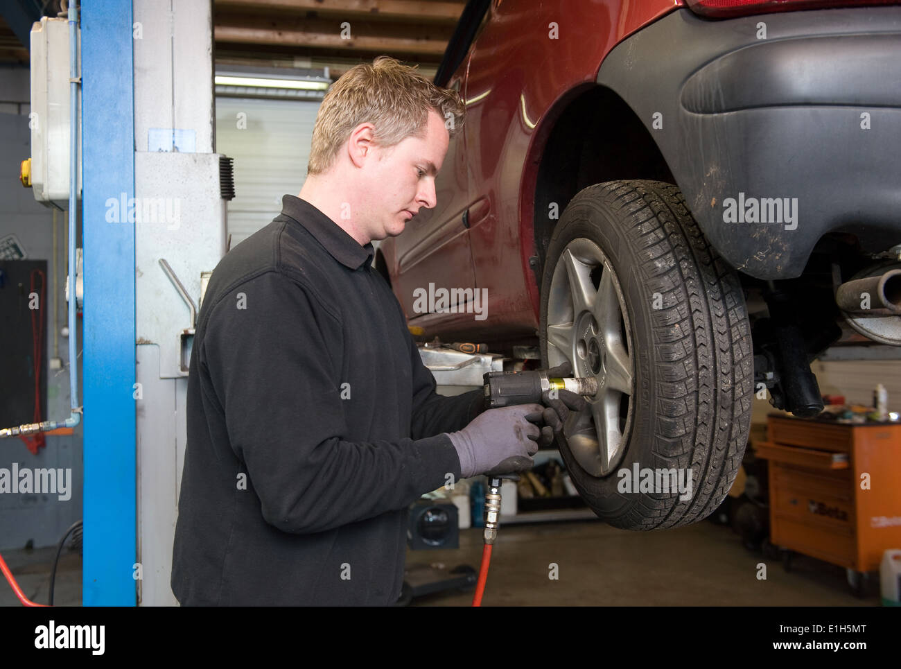 A mechanic is working on the wheel of a car who is lifted up in a ...