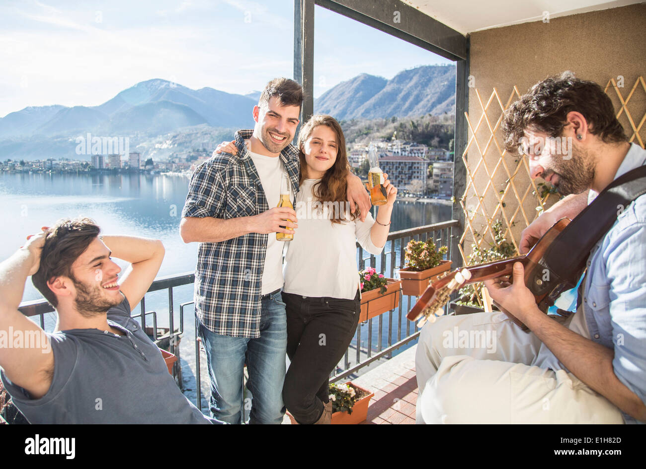 Four friends on balcony, with guitar and beer Stock Photo - Alamy
