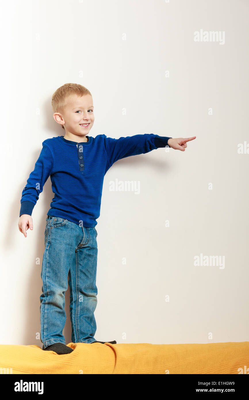 Little happy and smiling boy child standing on the couch and pointing ...