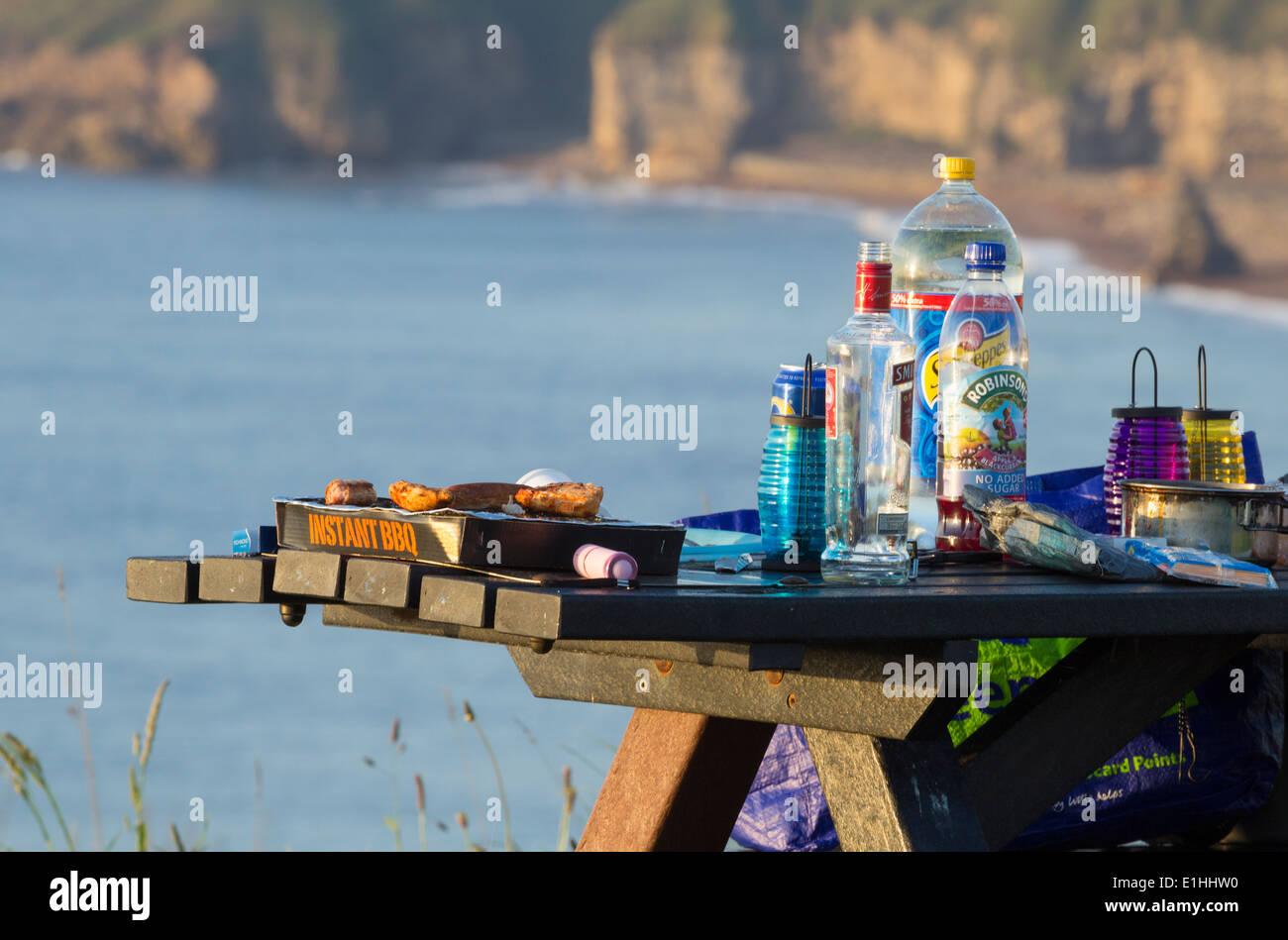 Instant BBQ and empty Vodka bottle on picnic table overlooking the sea ...