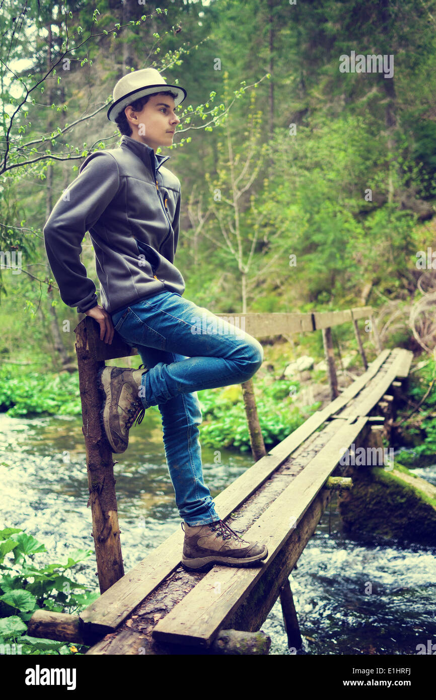 Portrait of a trendy teenager boy in hat outdoor on a wooden bridge ...