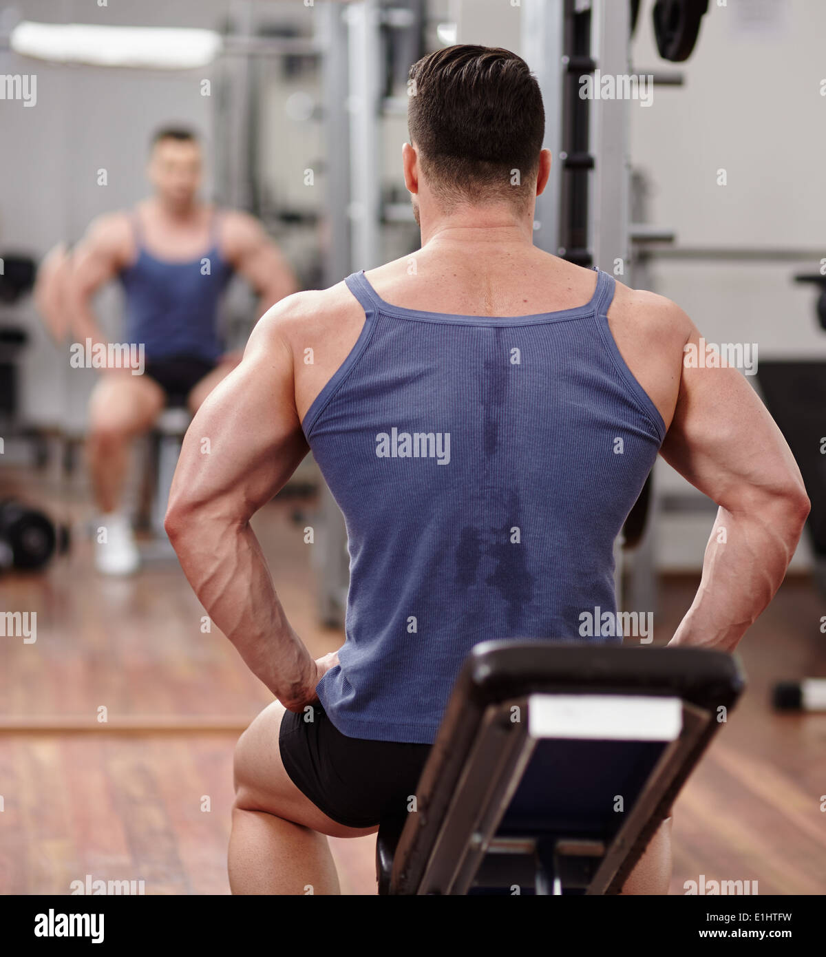 Strong athletic man in gym looking at his reflection in the mirror and ...