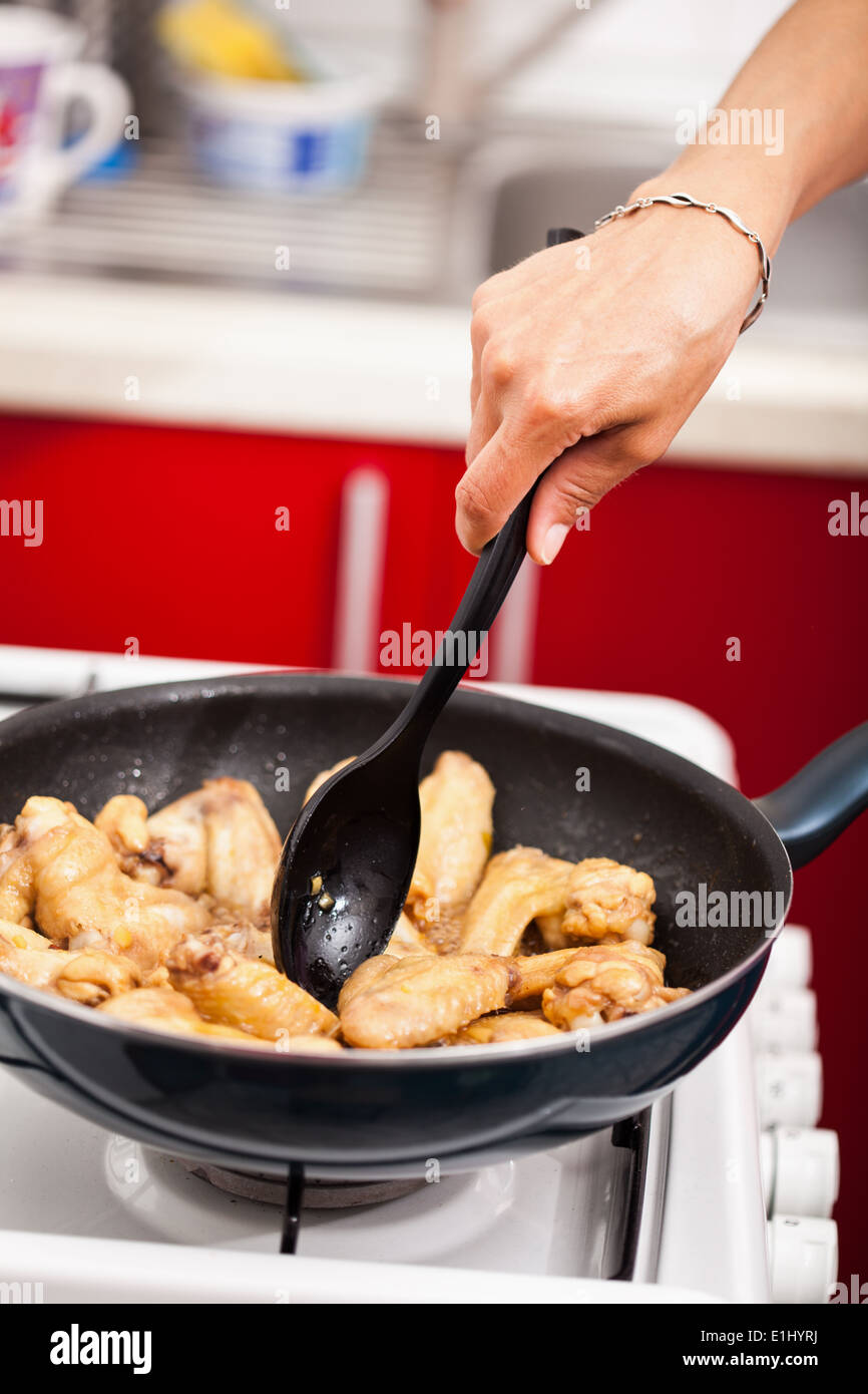 Woman's hand stirring in a wok chicken wings after an asian recipe ...