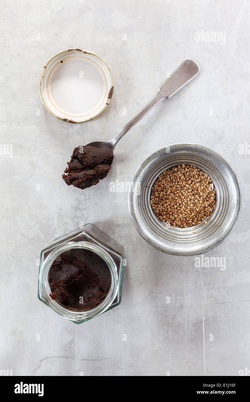 Glass and spoon of miso paste and bowl of roasted sesame, elevated view ...