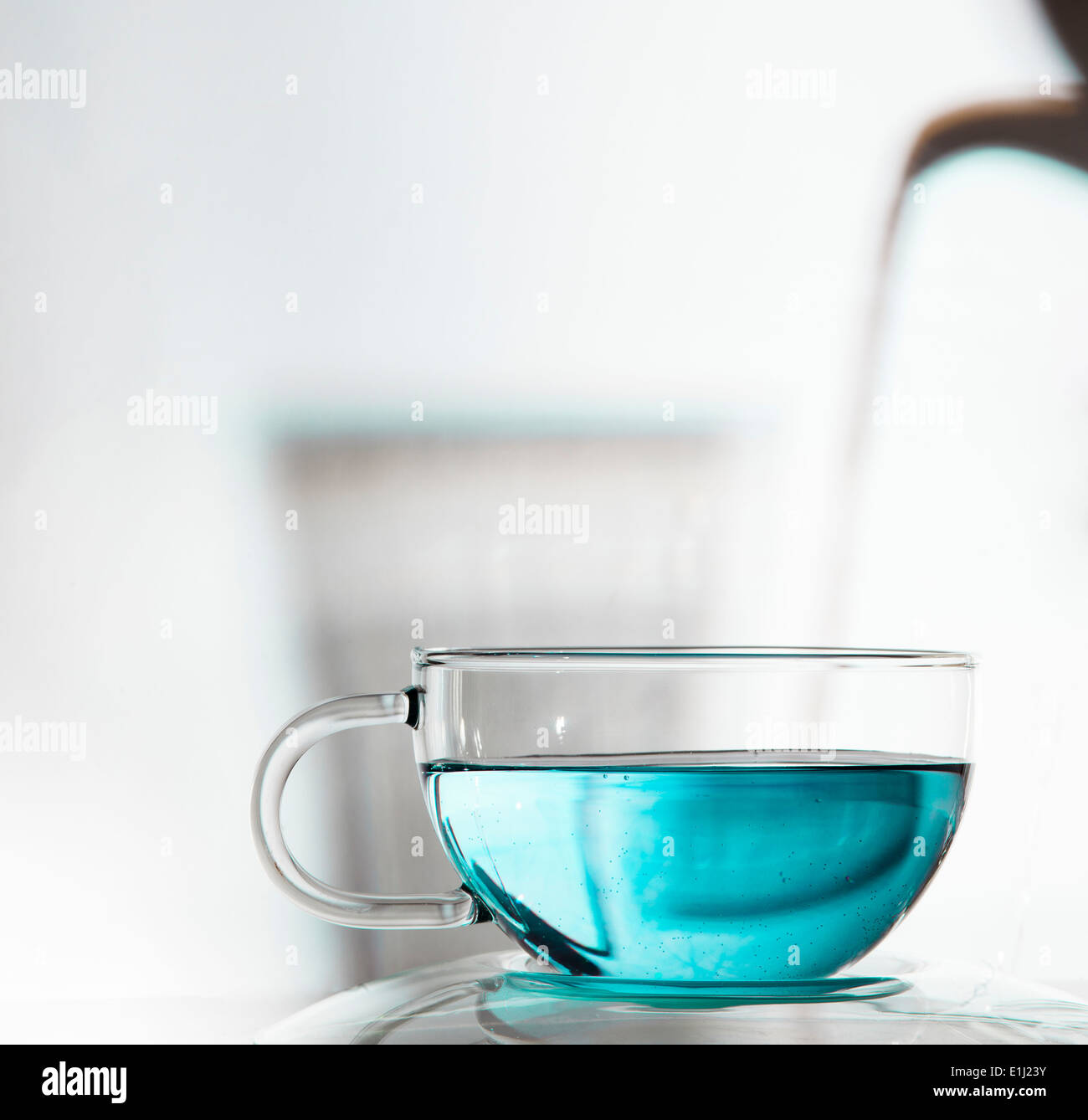 Transparent tea cup of light blue liquid in front of white background ...