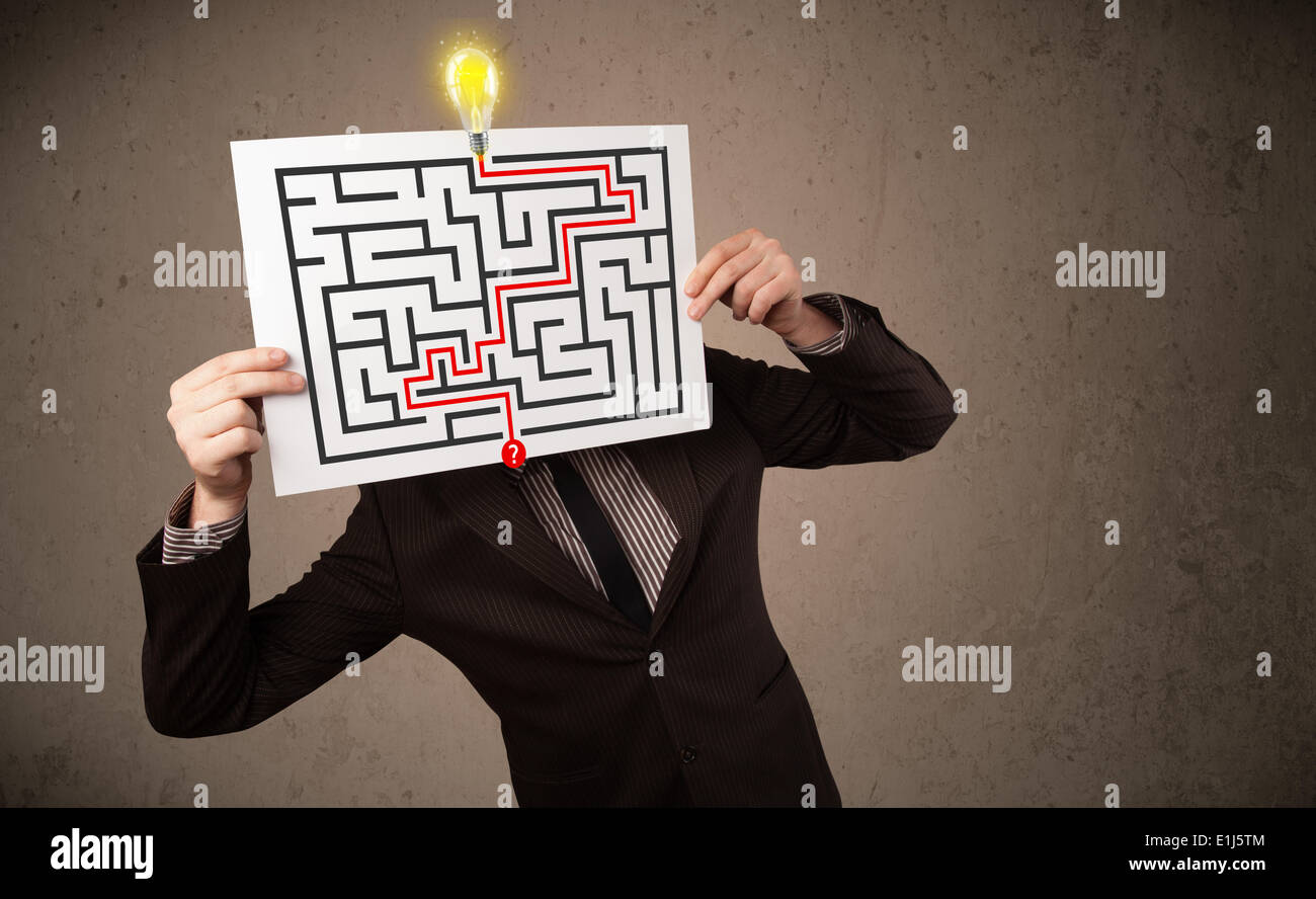 Businessman holding a paper with a labyrinth on it in front of his head ...