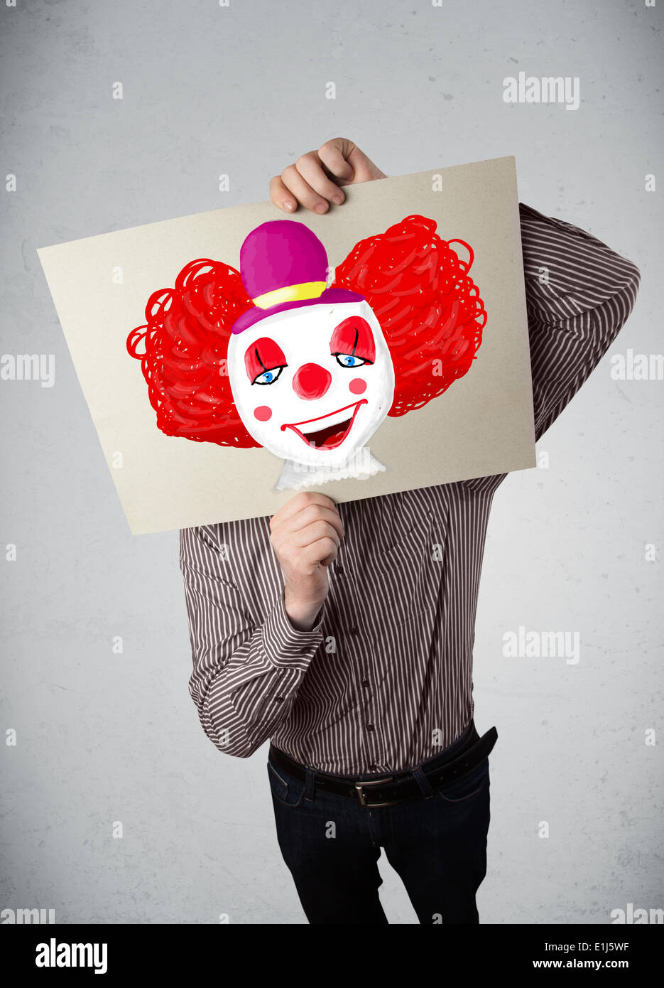 Businessman holding a cardboard with a clown on it in front of his head ...
