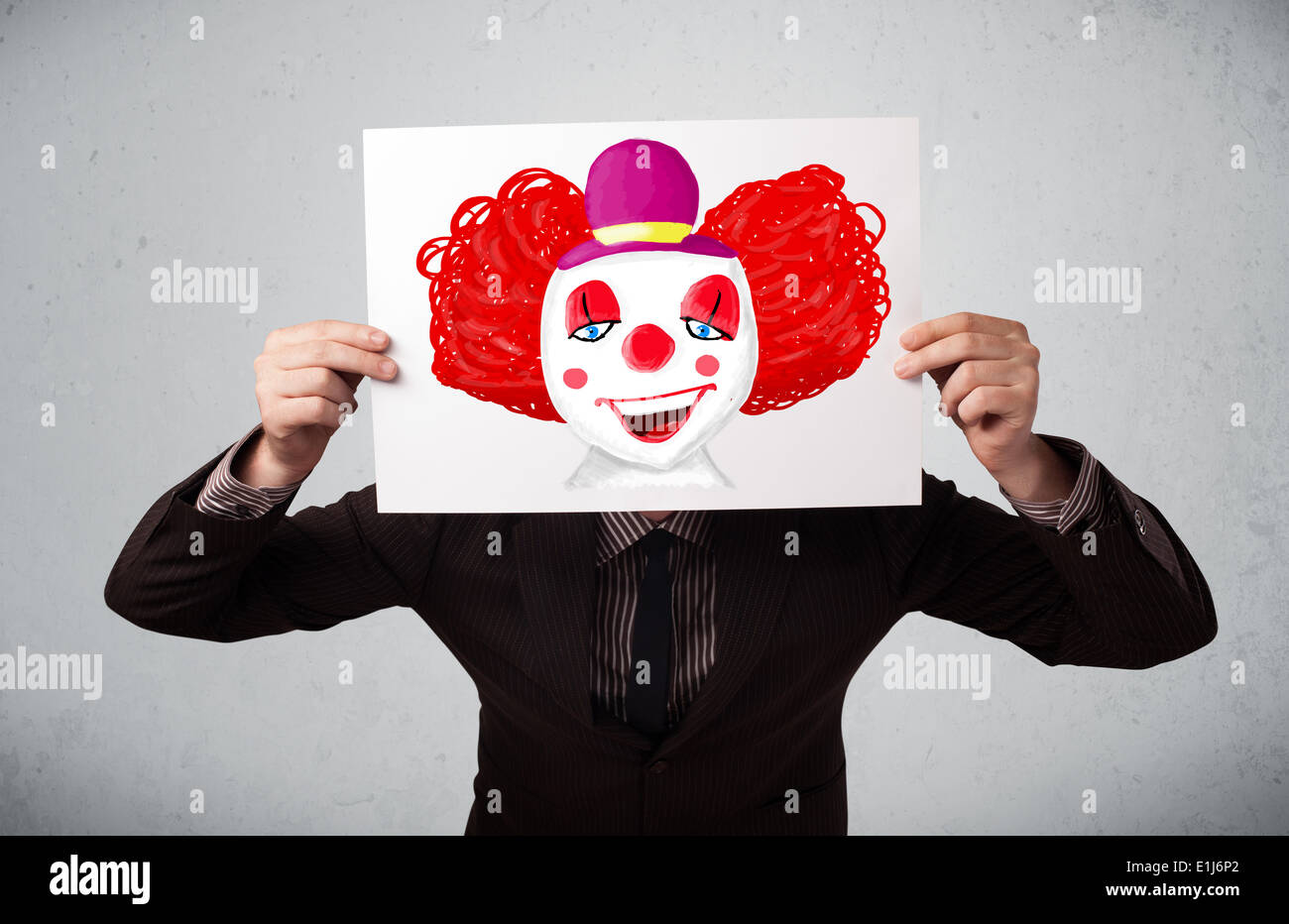 Businessman holding a cardboard with a clown on it in front of his head ...